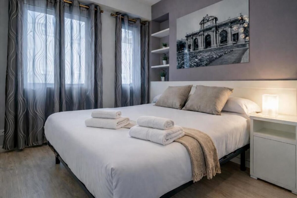 Cama bem arrumada com toalhas, abajur e um quadro na parede.