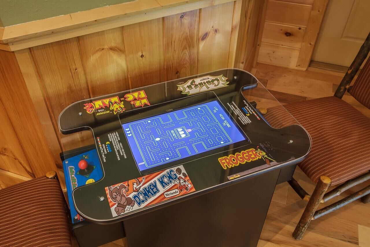 Máquina de jogos de fliperama antiga com tela azul, rodeada por lambris de madeira e duas cadeiras listradas.