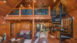 Interior de uma cabana de madeira, com sala de estar, cozinha e escada em espiral.