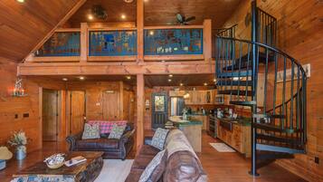 Interior de uma cabana de madeira, com sala de estar, cozinha e escada em espiral.
