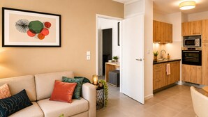 Sala de estar com sofá, mesa de centro com revista, quadro decorativo e cozinha com armários de madeira e eletrodomésticos.