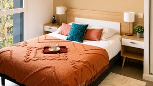 Quarto moderno com uma cama grande, mesas de cabeceira, um candeeiro suspenso e uma obra de arte emoldurada na parede.