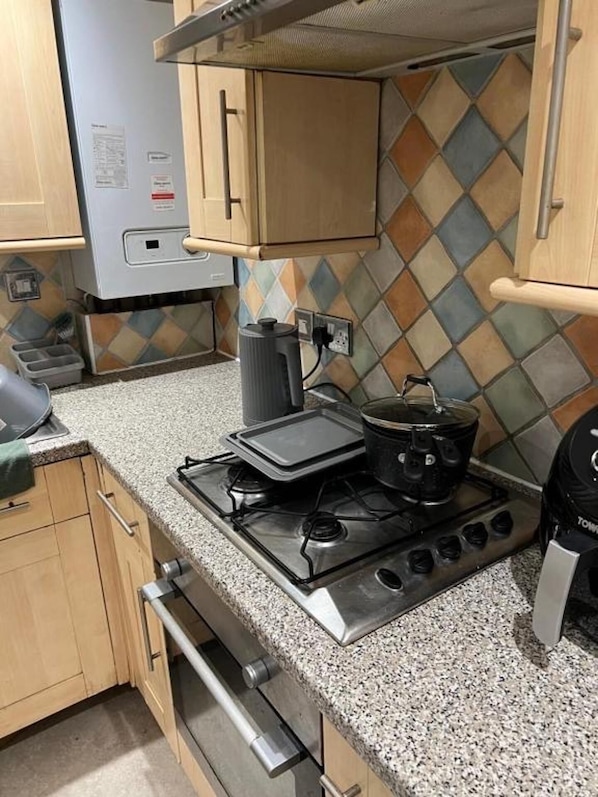 Uma cozinha com fogão a gás, chaleira e torradeira na bancada.