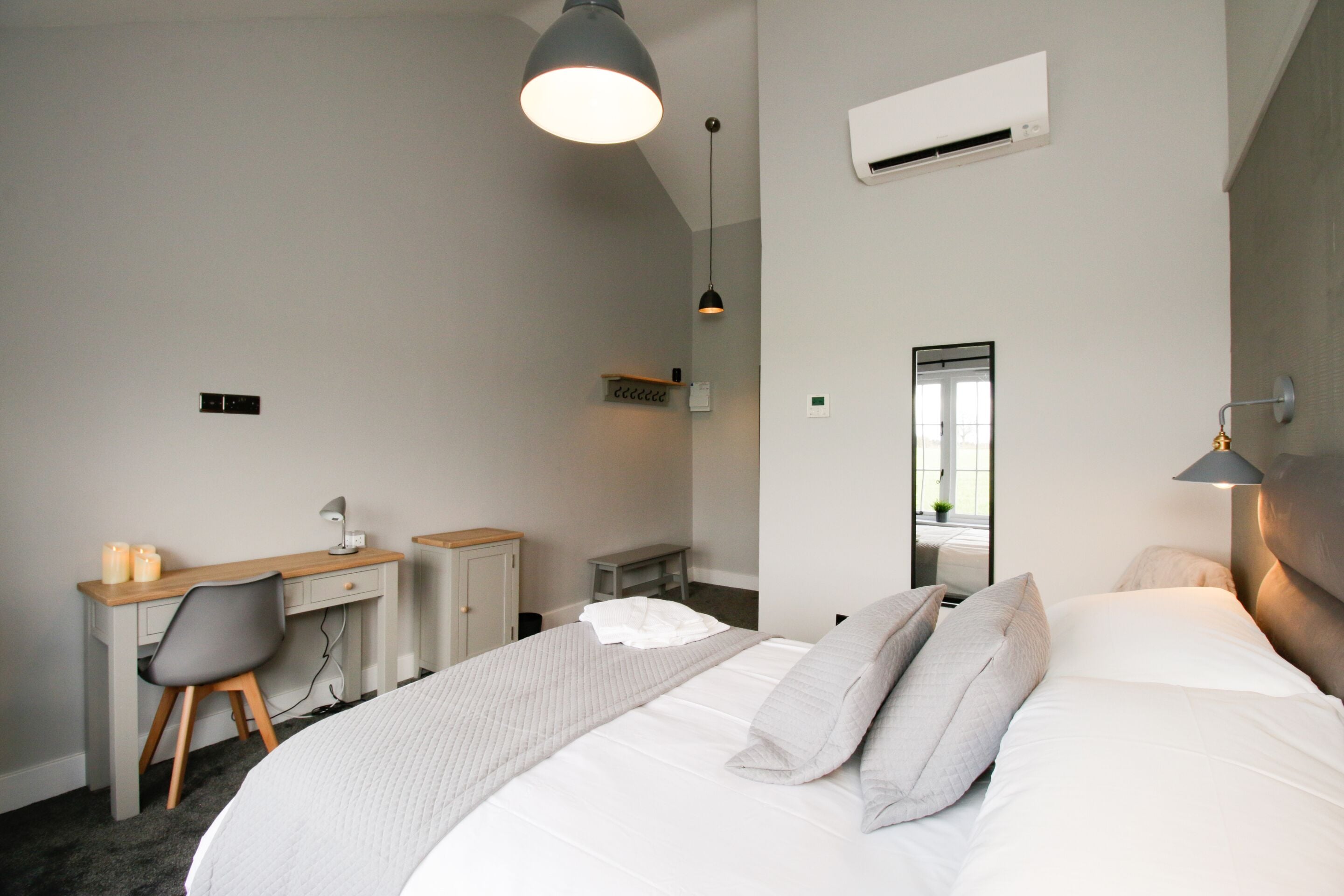 Quarto de hotel moderno com uma cama grande, uma escrivaninha, uma cadeira, um abajur e um aparelho de ar condicionado.
