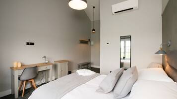 Quarto de hotel moderno com uma cama grande, uma escrivaninha, uma cadeira, um abajur e um aparelho de ar condicionado.
