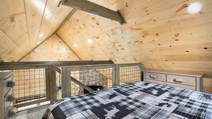 Interior de uma cabana de madeira com cama, janela e escada.