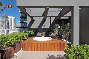 Um terraço no telhado com um deck de madeira, uma banheira de hidromassagem e vasos de plantas.