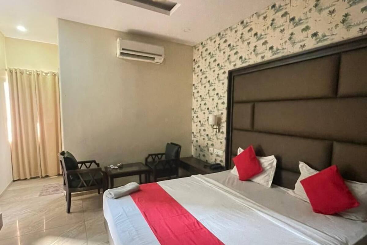 Quarto de hotel com cama, escrivaninha, cadeira, ventoinha no teto e janela com cortinas.