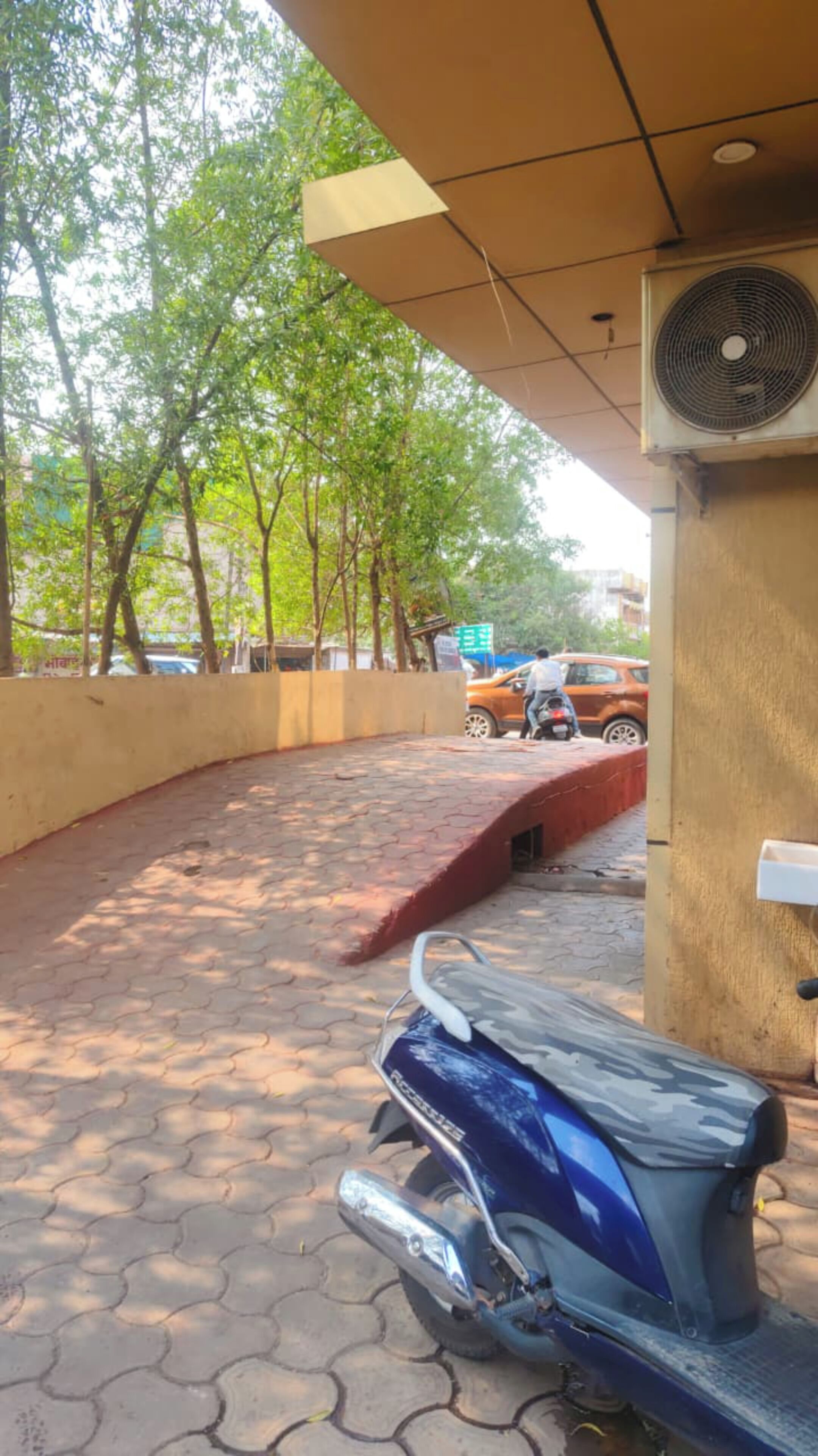 Uma área pavimentada com uma scooter, uma borda vermelha e um veículo ao fundo.