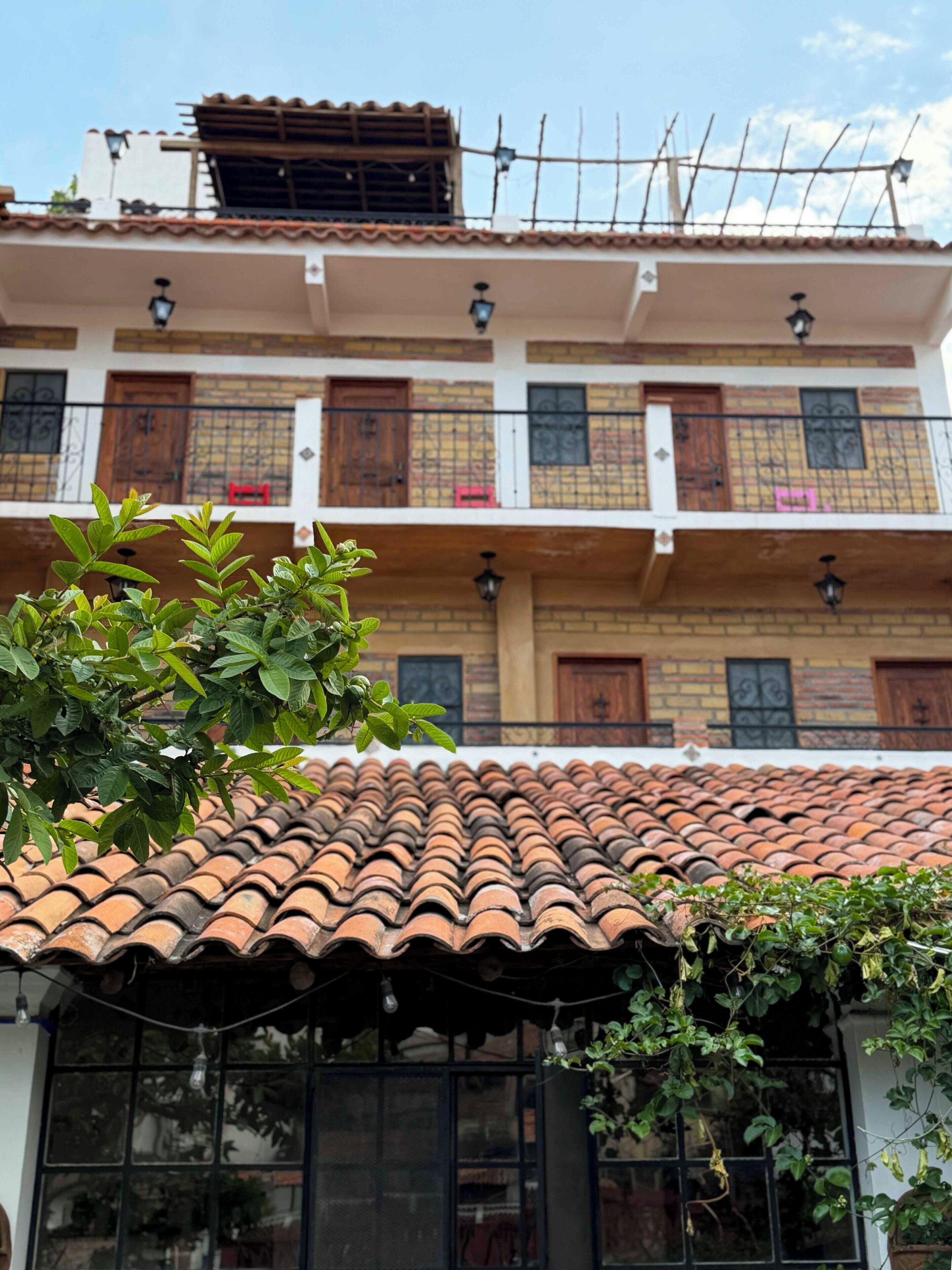 Um edifício de vários andares com telhado em telhas, varandas com grades de metal e janelas com grades decorativas.