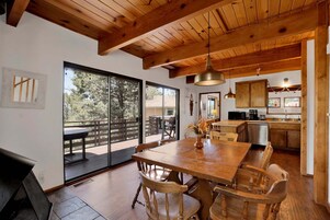 Uma sala de jantar espaçosa com mesa e cadeiras de madeira, uma cozinha com armários de madeira e uma grande porta de vidro deslizante que dá para um deck externo.