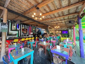 Um restaurante com teto de madeira rústica, cadeiras coloridas e mesas.