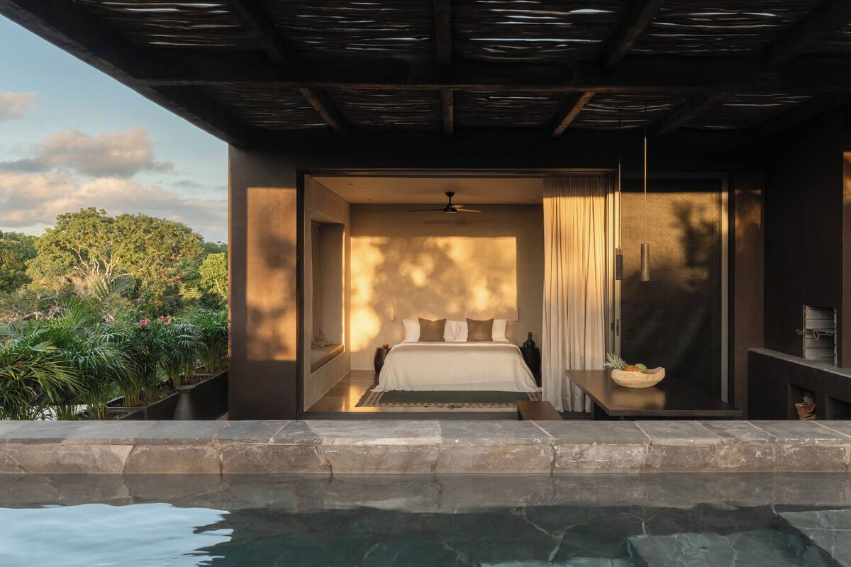 Quarto moderno com cama, mesa de cabeceira e vista para uma piscina.