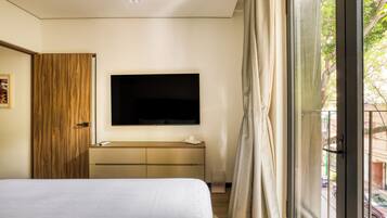 Quarto com cama, televisão na parede, guarda-roupa de madeira e janela com cortinas.