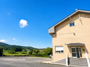Um edifício com teto plano, entrada frontal com porta de vidro e estacionamento em frente.