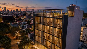 Um edifício alto com vários andares, grandes janelas e um terraço no telhado.