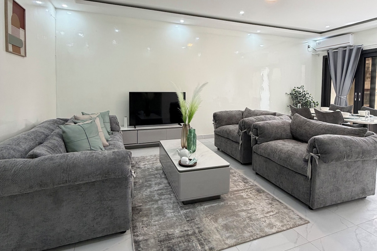 Uma sala de estar moderna com sofás cinza, uma mesa de centro e uma televisão de tela plana.