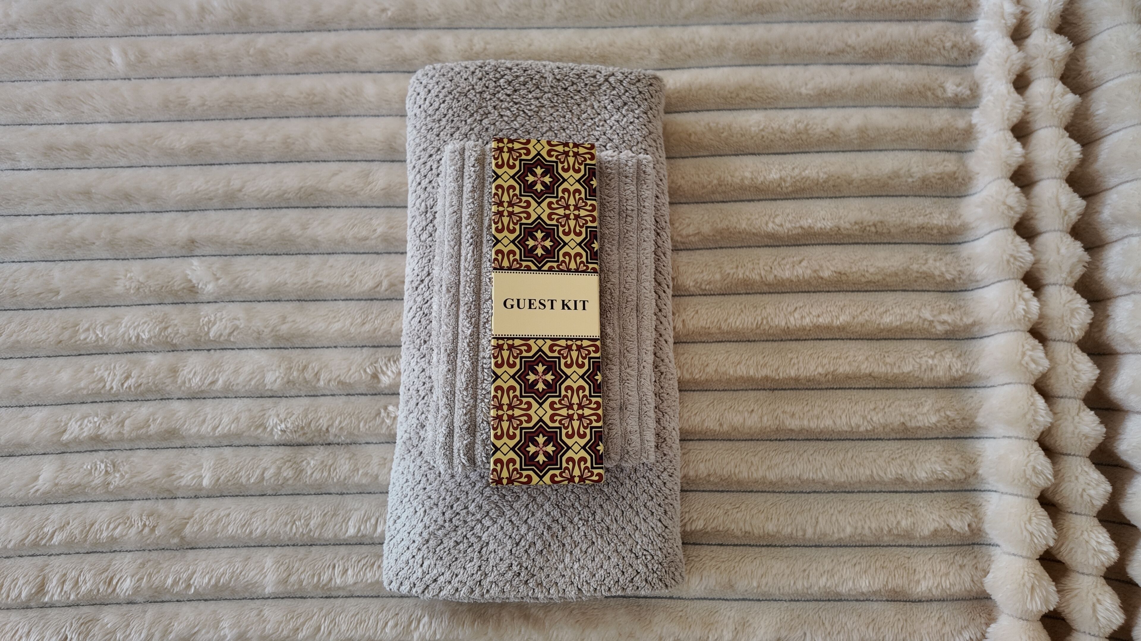 Uma toalha dobrada com um etiqueta 'GUEST KIT' sobre uma superfície texturizada e listrada.