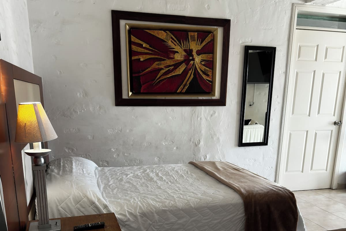 Quarto de hotel com duas camas, abajur, quadro na parede, espelho e uma porta.