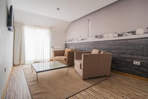 Uma sala de estar com um mural da paisagem urbana, uma televisão de tela plana e uma mesa de centro de vidro.
