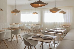 Uma sala de jantar moderna com mesas redondas, cadeiras brancas e luminárias pendentes.
