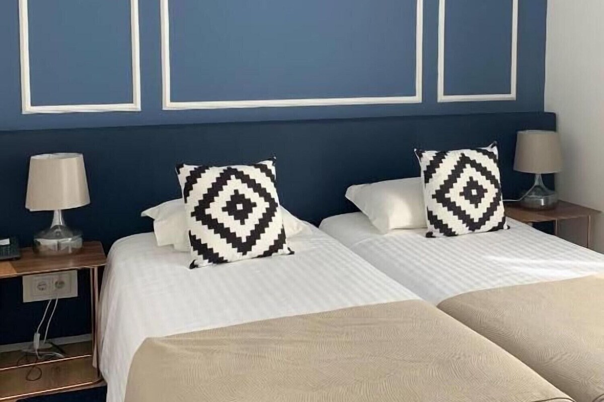 Quarto de hotel com uma cama, duas mesas de cabeceira e uma parede com três molduras retangulares.