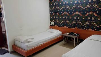 Uma cama de solteiro com estrutura de madeira, uma mesa de cabeceira com telefone e um ar condicionado fixado na parede.