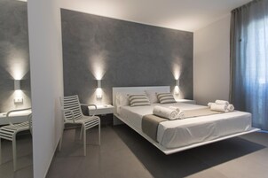 Quarto moderno com cama, mesas de cabeceira, uma cadeira e luminárias fixadas na parede.