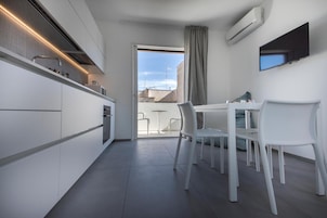 Uma cozinha moderna com armários brancos, uma área de jantar com mesa e cadeiras, e uma TV fixada na parede.