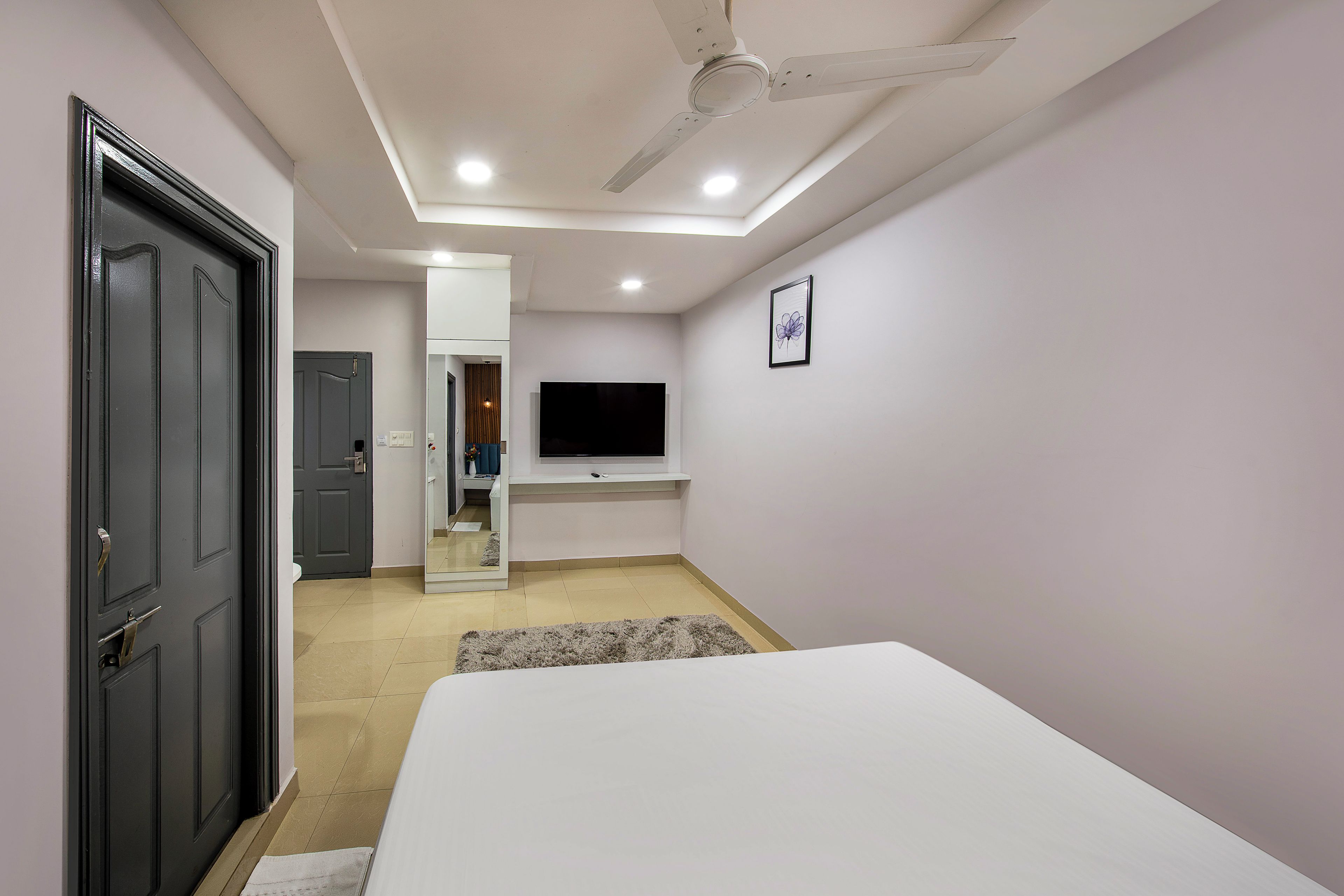Um quarto moderno com uma cama, ventoinha no teto, iluminação embutida, televisão e um espelho.