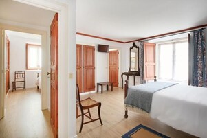 Quarto com cama, guarda-roupa de madeira, uma mesinha, uma cadeira e uma televisão.