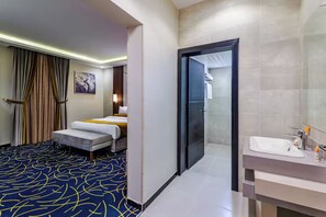Quarto de hotel com cama, banheiro com pia e porta que dá para outro cômodo.