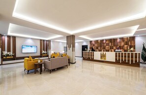 Um saguão moderno de hotel com balcão de recepção, área de estar e uma tela de televisão.