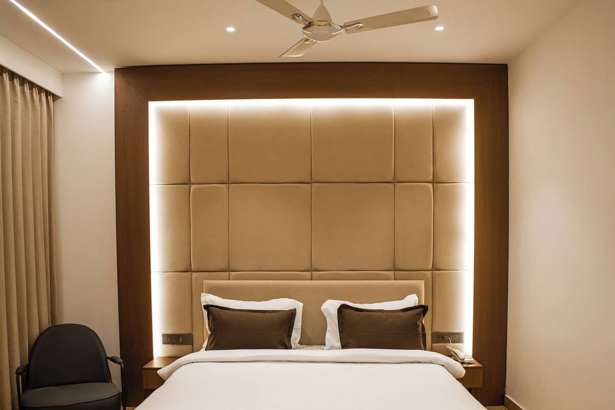 Quarto de hotel moderno com uma cama grande, ventoinha no teto e piso de madeira.