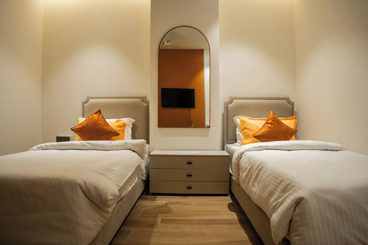 Quarto de hotel com duas camas, uma TV de tela plana fixada na parede e um espelho sobre a cômoda.