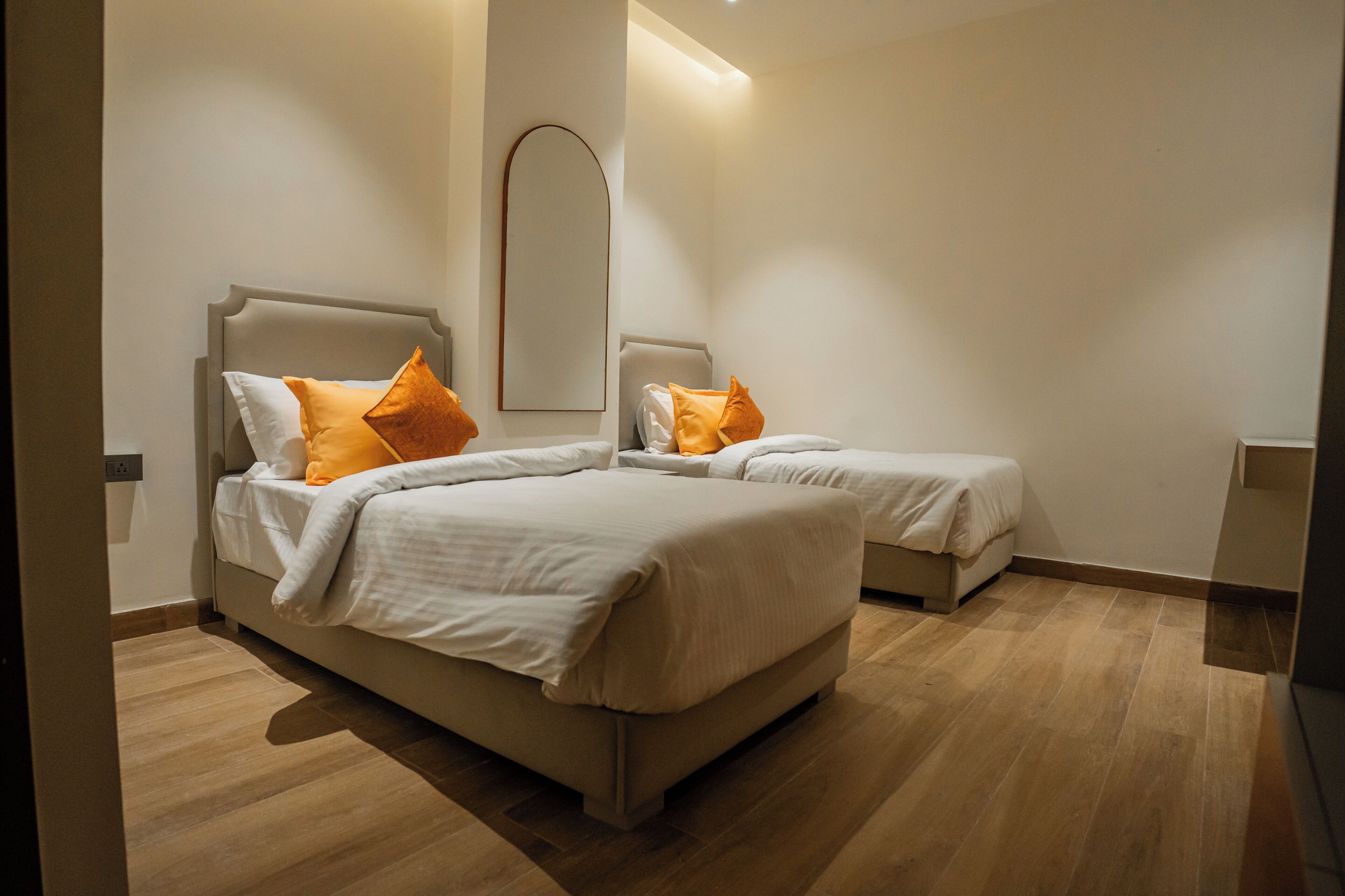 Quarto de hotel com duas camas, um espelho grande e piso de madeira.