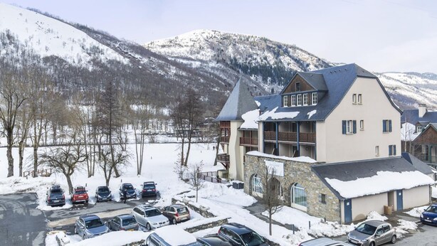 Um hotel com fachada de pedra, várias varandas e um estacionamento com carros.