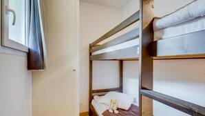 Quarto com beliche, janela, porta e piso de madeira.