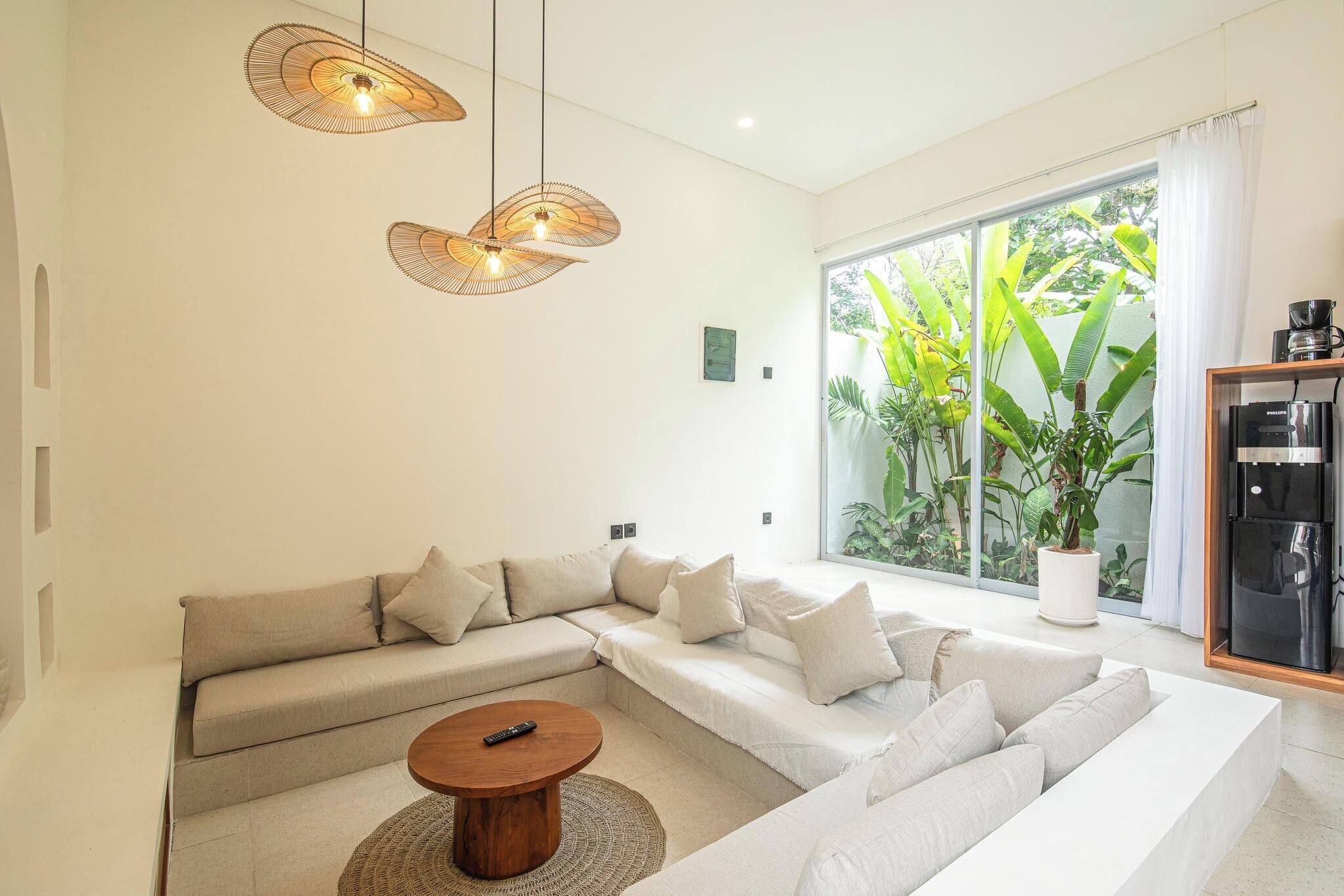 Uma sala de estar moderna com sofá seccional, mesa de centro e janelas amplas com vista para vegetação.