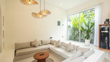 Uma sala de estar moderna com sofá seccional, mesa de centro e janelas amplas com vista para vegetação.