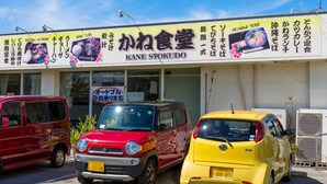Um edifício com uma placa indicando 'KANE SYOKUDO' e três carros estacionados na frente.