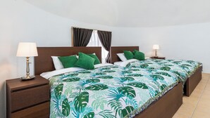 Quarto com cama, duas mesas de cabeceira, um criado-mudo, janela com cortinas e uma luminária na parede.