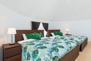 Quarto com cama, duas mesas de cabeceira, um criado-mudo, janela com cortinas e uma luminária na parede.