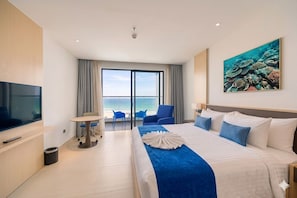 Quarto de hotel com cama, televisão, varanda e vista para o oceano, e uma pintura de corais.