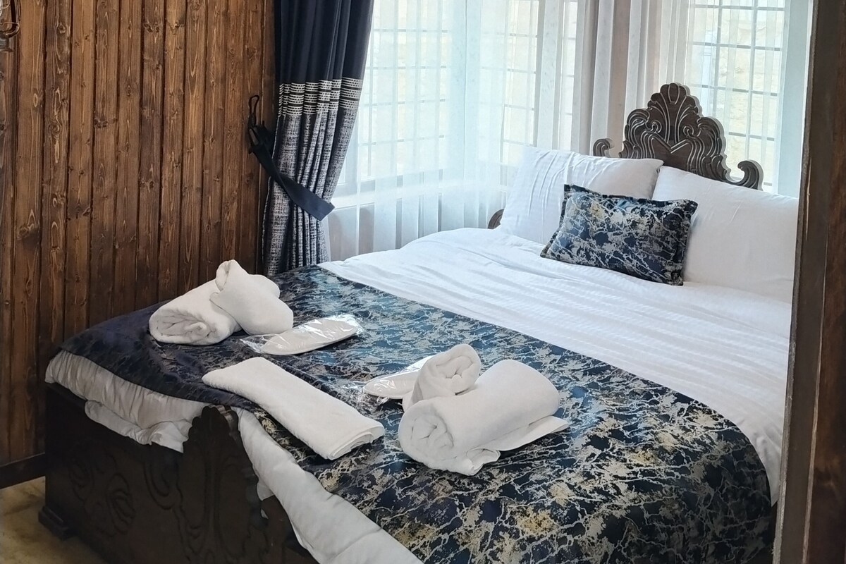 Um quarto com uma cama, parede de madeira, janela com cortinas e luminária no teto.