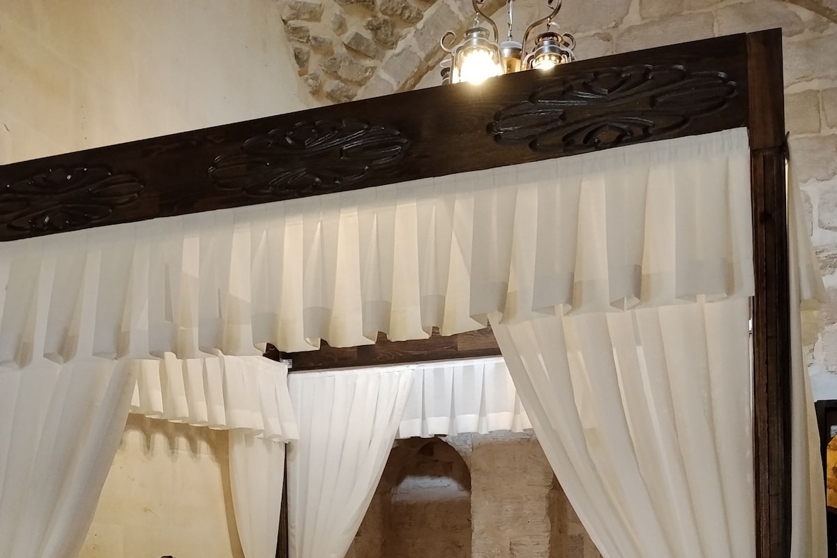 Uma cama com dossel, roupa de cama branca e vermelha, uma parede de pedra e uma cabeceira de madeira.