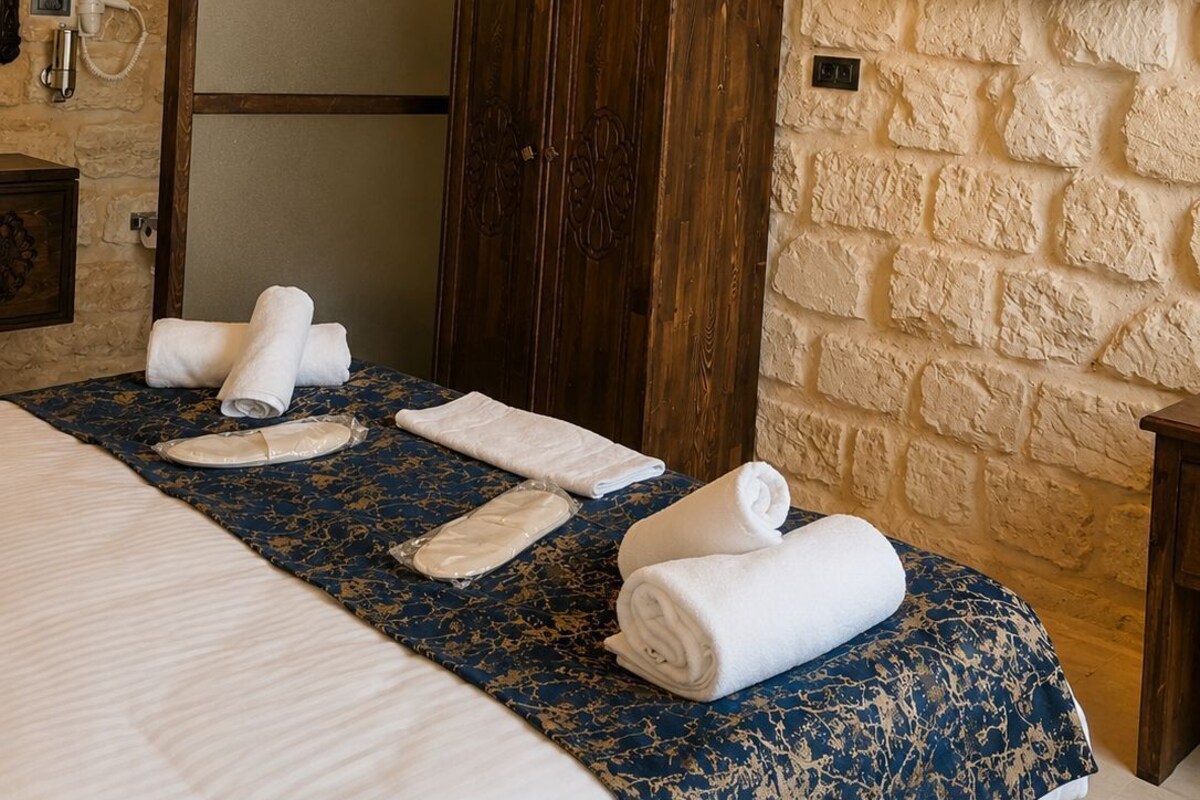 Quarto de hotel com uma cama, um guarda-roupa de madeira, uma televisão na parede e uma parede de pedra.