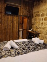 Quarto com cama, guarda-roupa de madeira, parede de pedra, pia e uma pequena mesa com um controle remoto.
