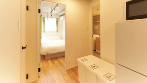 Um corredor estreito com uma cama, um armário branco e um micro-ondas.