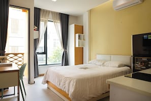Quarto de hotel com cama, escrivaninha, cadeira, mesa pequena, geladeira e janela com cortinas.